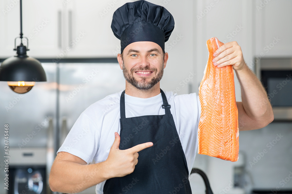 Millennial hispanic man in chef uniform hold fish salmon at kitchen ...
