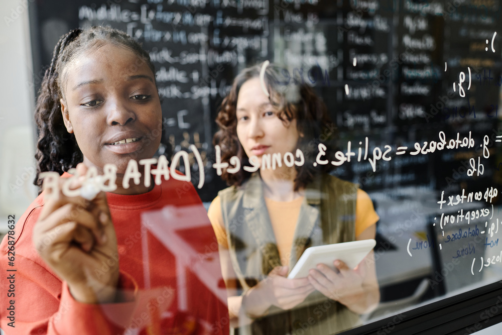 African American teacher writing codes on blackboard and explaining IT ...