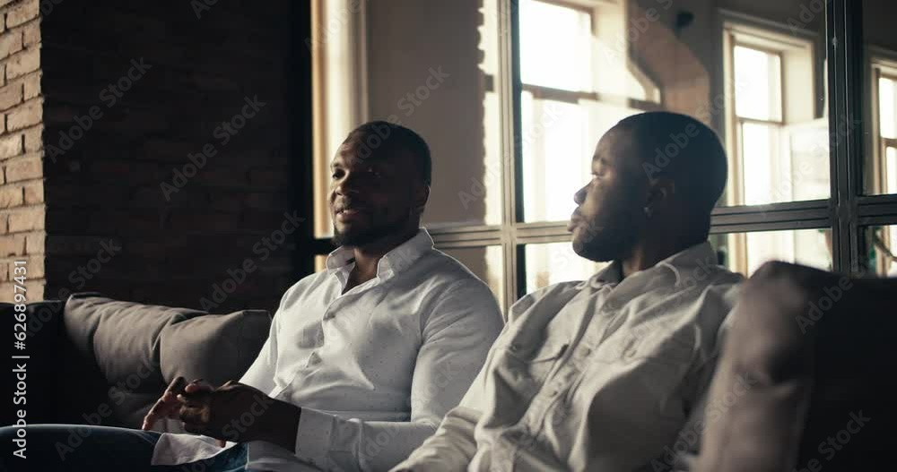 Two businessmen are sitting in a loft-style sunny office and chatting ...