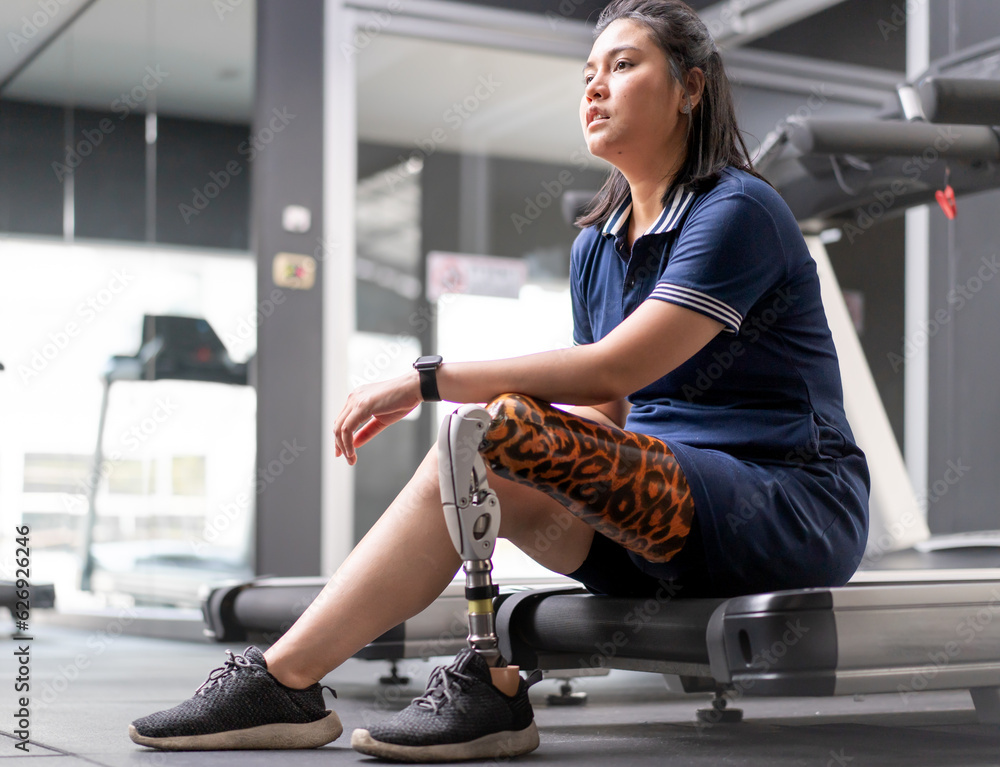Woman with prosthetic leg sits isolated in gym. Asian female with foot ...