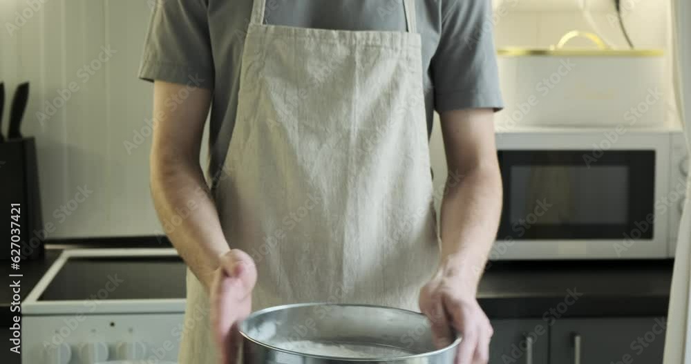 Portrait of a man as he delicately sieves flour through a sieve. The ...