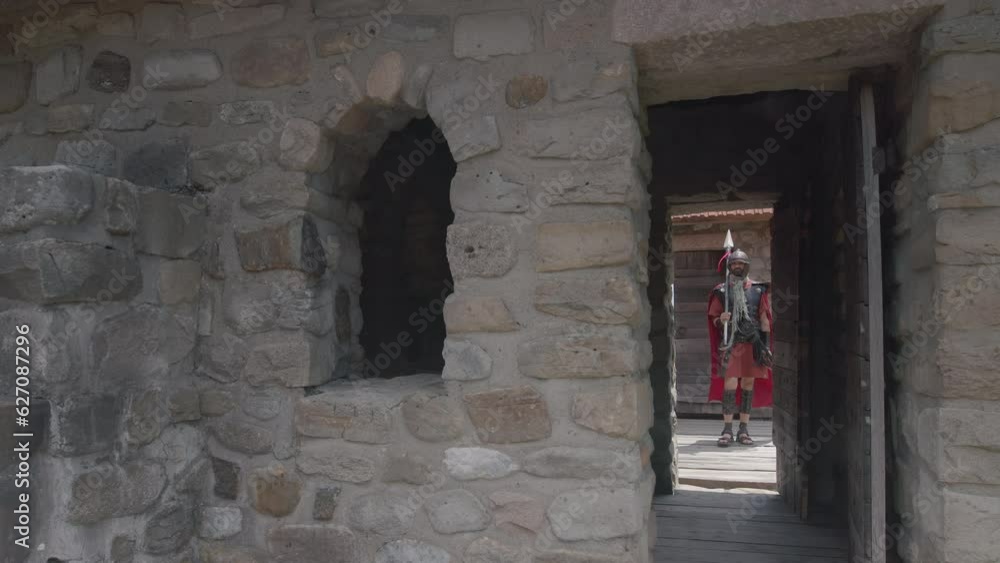 Roman soldier patrols with a spear on a fort wall. View through wooden ...