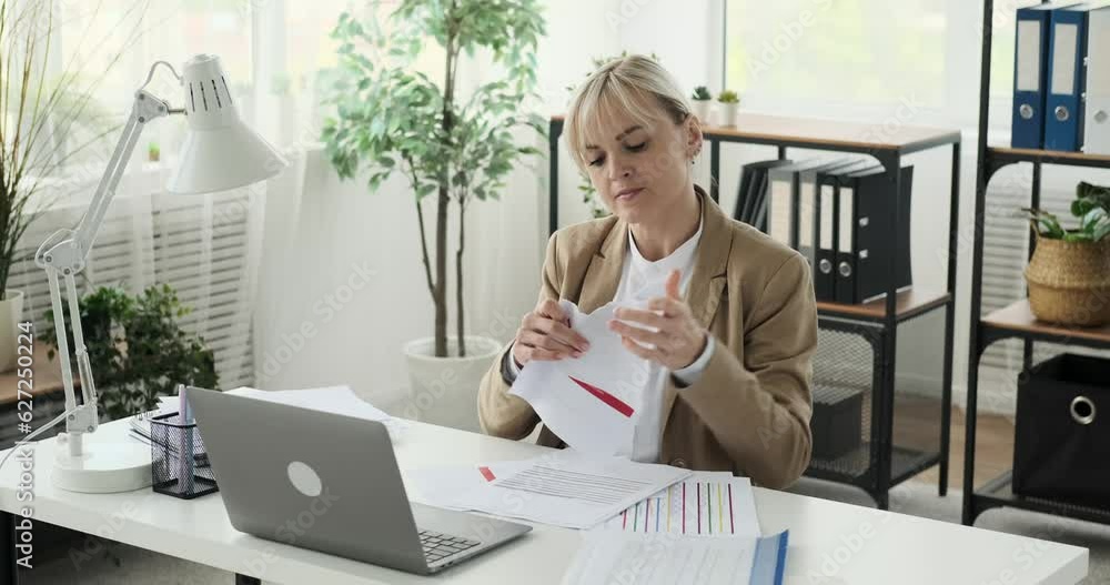 Frustrated businesswoman is seen ripping papers at her desk. Her facial ...