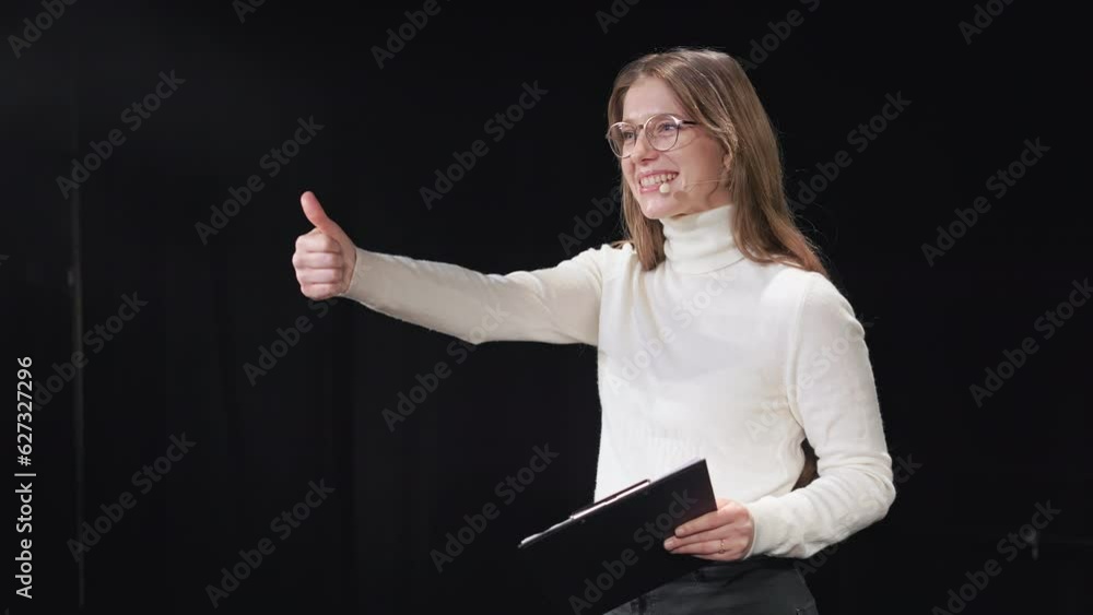 Female conference presenter in headset doing happy thumbs up gesture ...