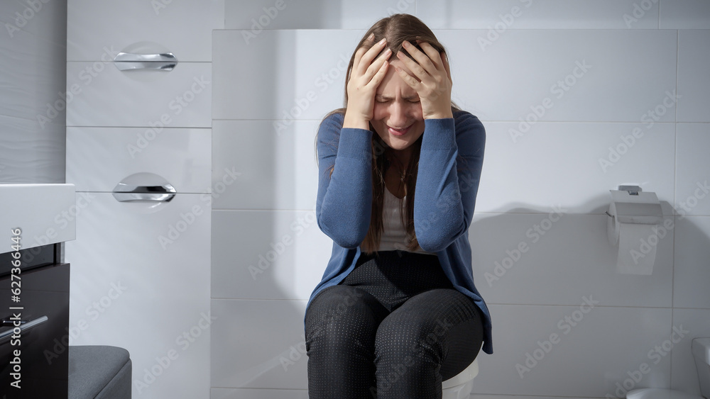 Foto de Young upset woman sitting on toilet alone and crying. Concept ...