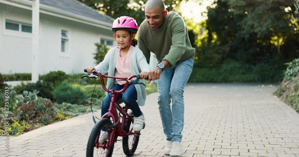Father helping his kid to ride a bicycle in a green garden on a weekend ...