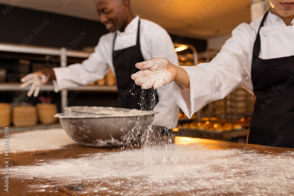 Happy diverse bakers working in bakery kitchen, pouring flour and ...