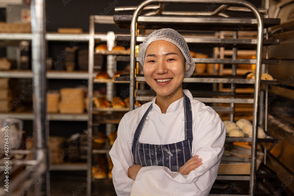 Portrait of happy asian female baker in bakery kitchen wearing apron ...