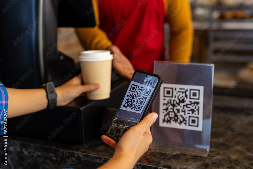 Diverse male bakery worker and customer scanning qr code with ...