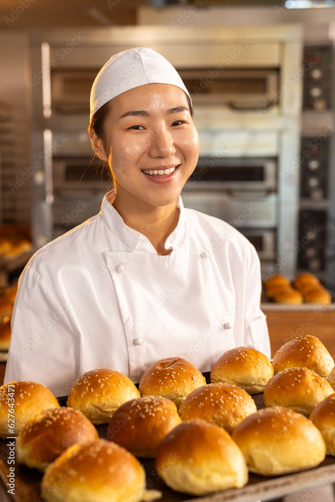 Portrait of happy asian female baker in bakery kitchen presenting fresh ...