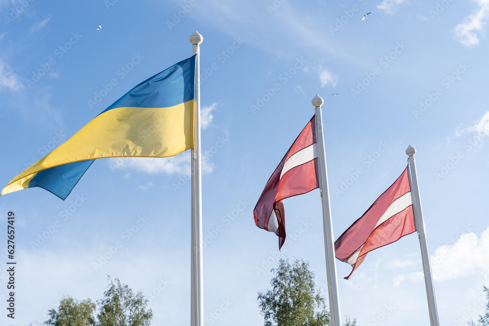 Ukrainian and Latvian flags together on flag poles waving in wind Stock ...