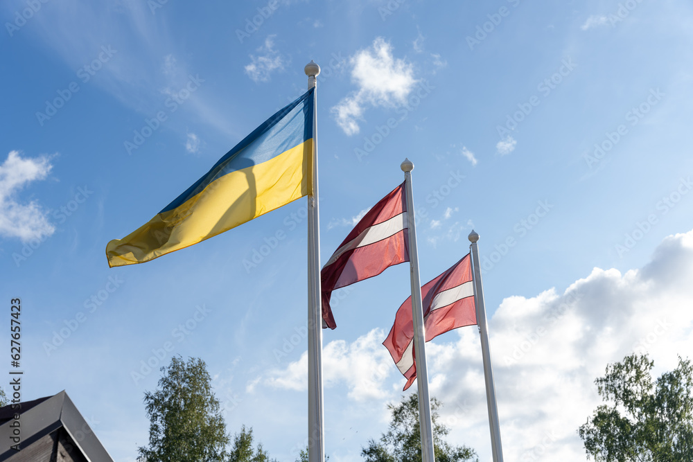 Ukrainian and Latvian flags together on flag poles waving in wind Stock ...
