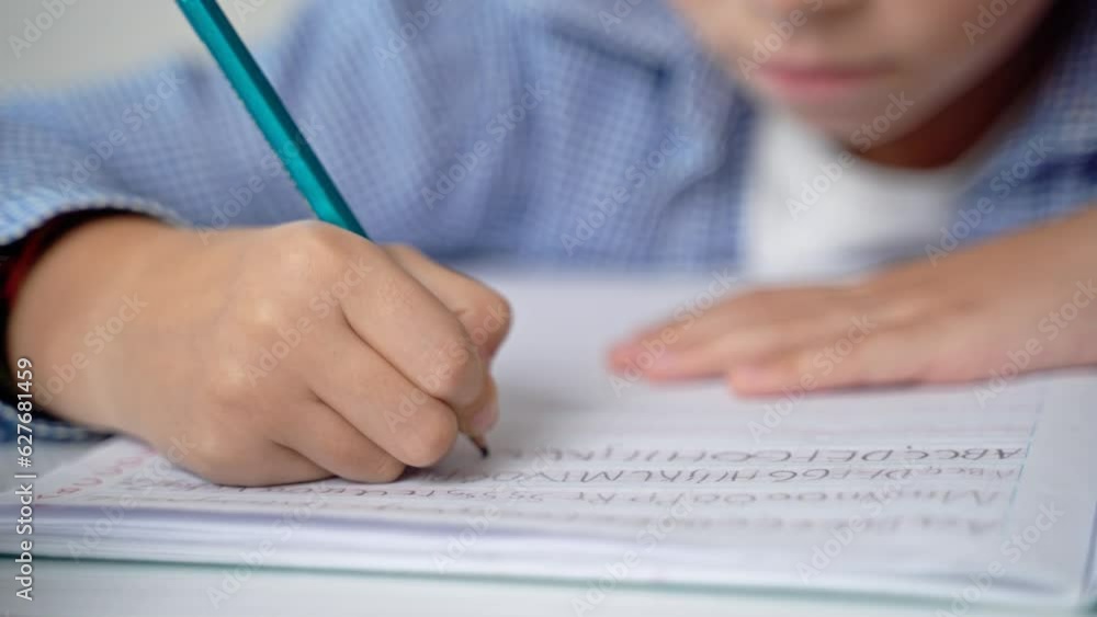 Elementary school student boy or girl writing letters, studying at desk ...