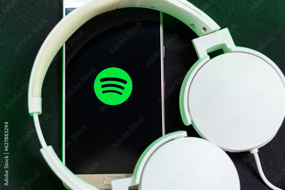 A smartphone connected to white headphones using the Spotify app on a ...