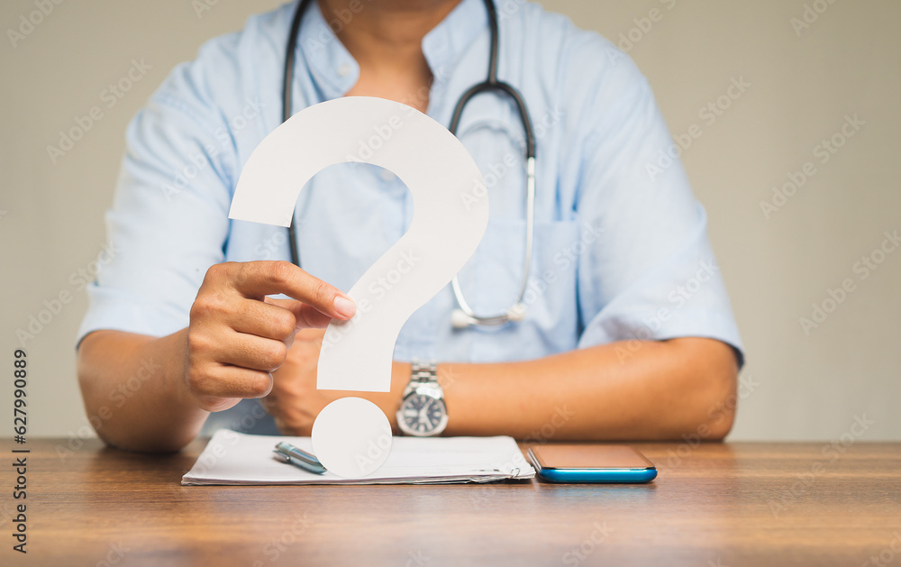 Physician holding a white question mark while sitting at the table in ...