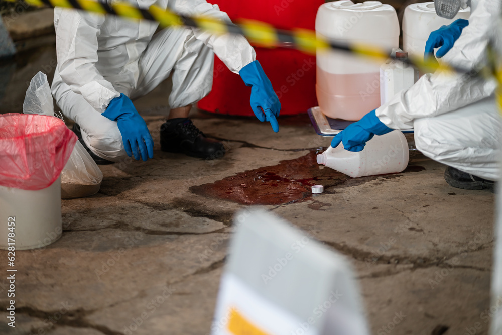 A team of two chemists, wearing PPE suits and gas masks, recover a ...