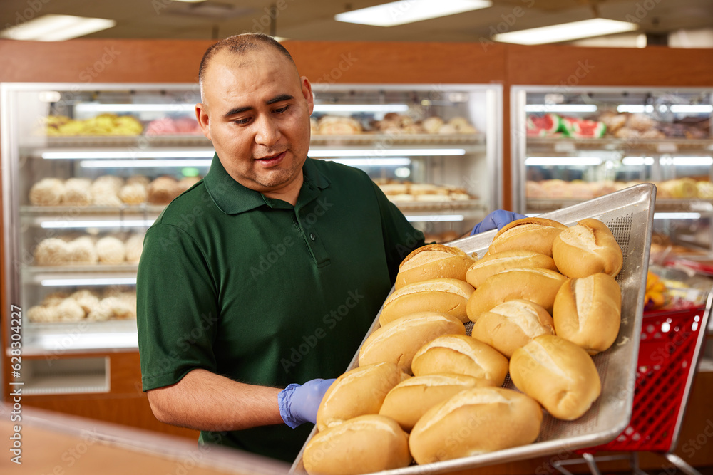 Baker in grocery store refilling bin with tray of fresh baked Bolillos ...