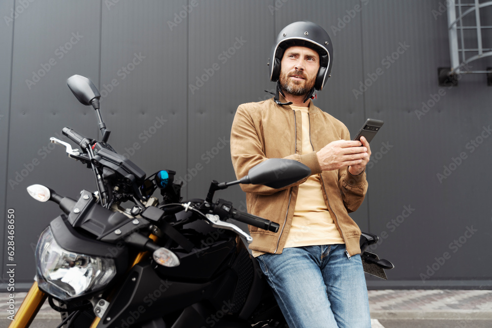 Stylish confident man, biker wearing helmet using mobile phone standing ...