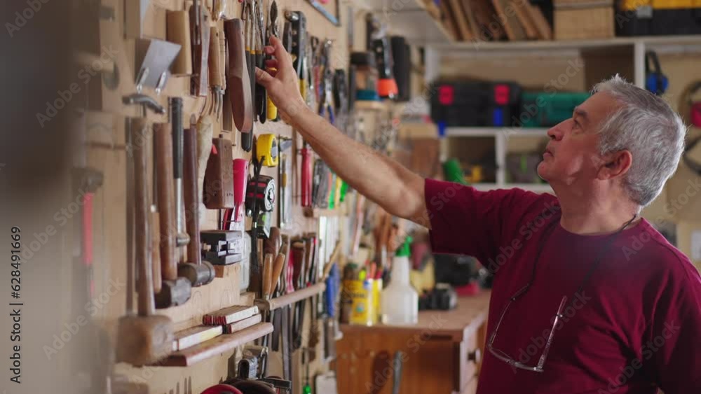 Older man working at workshop, grabbing tools from wall and engaged ...
