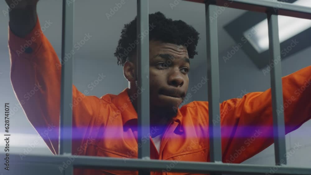 Sad African American man in orange uniform leans hands on prison cell ...