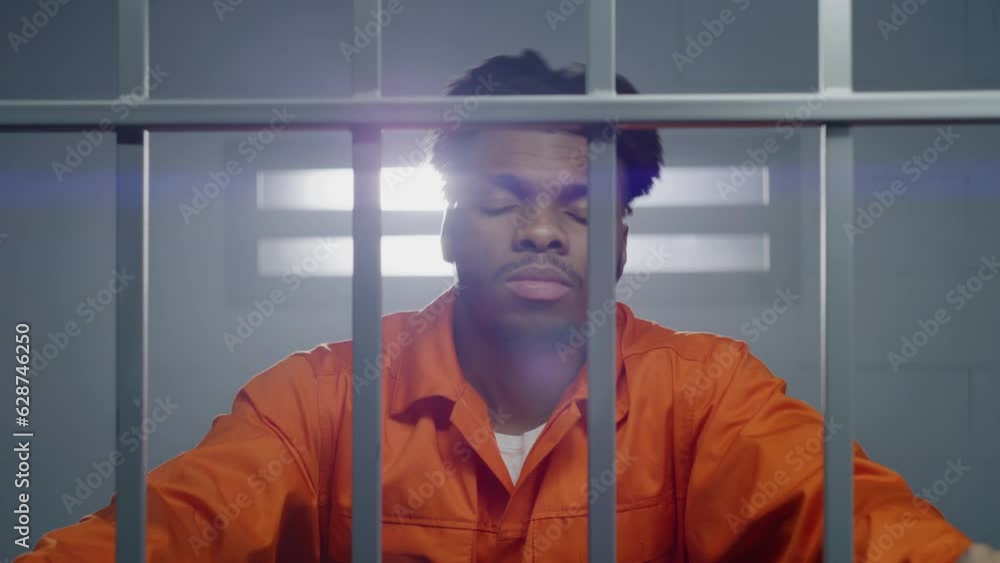 African American man in orange uniform looks at camera and kneads neck ...