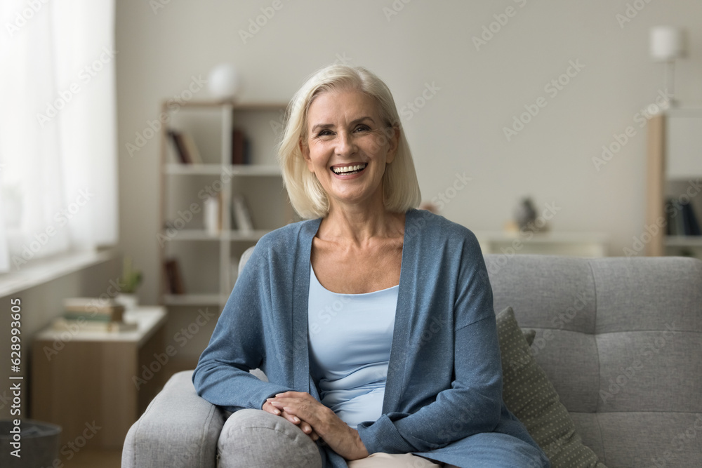 Happy pretty senior woman sitting on couch at cozy home, looking at ...