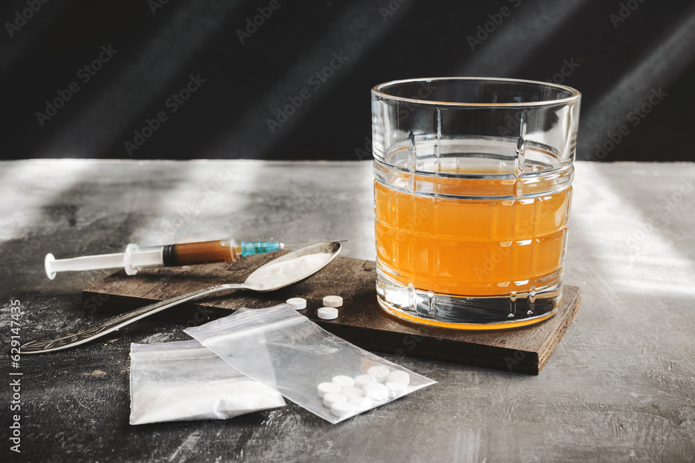 Alcohol drink in a glass, syringe with a dose of drugs, white pills and ...