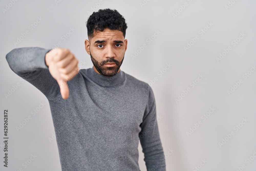 Hispanic man with beard standing over white background looking unhappy ...