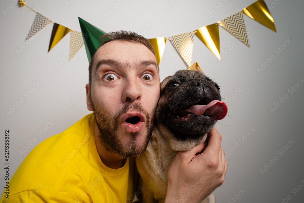 portrait of Funny guy with cute pug dog in a party hat hugging and ...