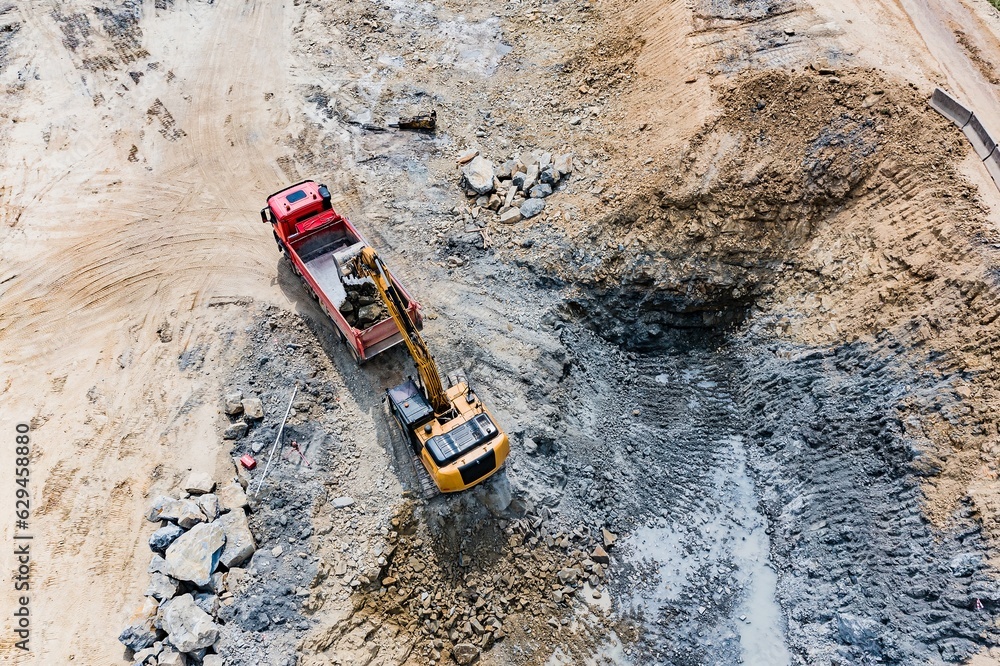 Excavator loading a truck with stones and road underlayment at a road ...