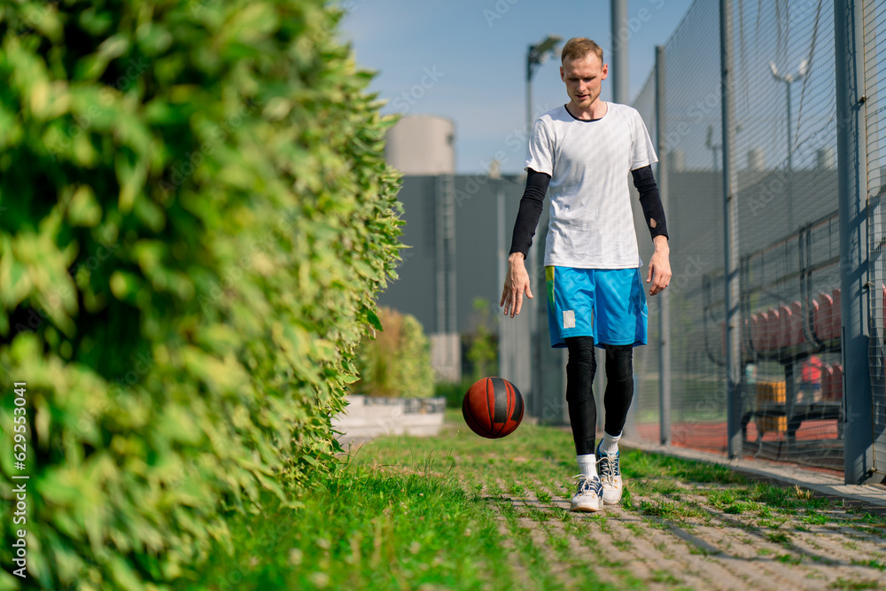 A tall guy basketball player walks down the park path to the basketball ...