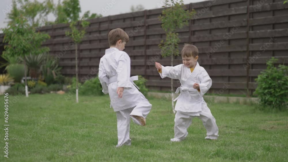Little cheerful funny kids playing karate in white suit in the garden ...