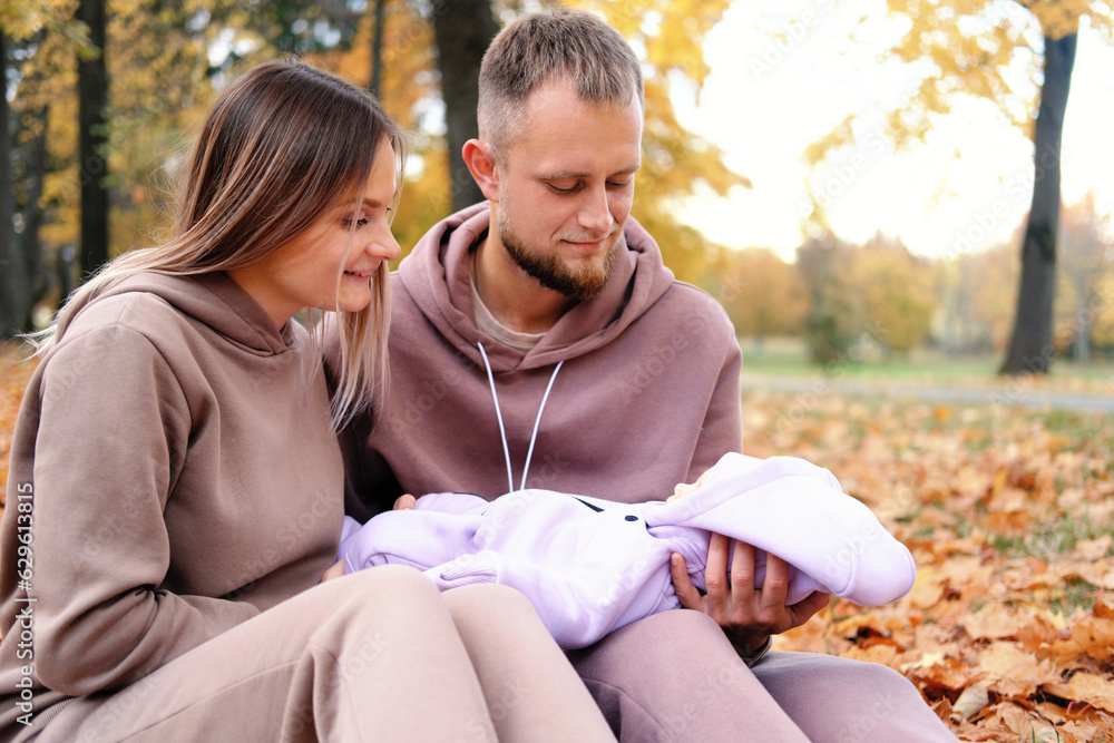 Young parents sit on a plaid with a newborn baby in an autumn park. The ...