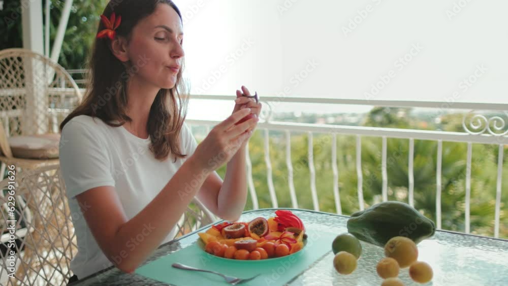 Woman eating tropical fruits sitting on the balcony with jungle view ...