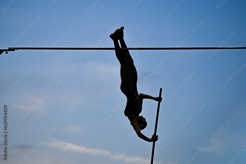 A female pole vaulter (silhouette) jumping with a beautiful blue sky in ...