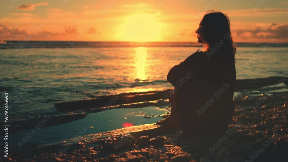 Woman sitting on beach looking at sunset sky and ocean waves. Dreaming ...