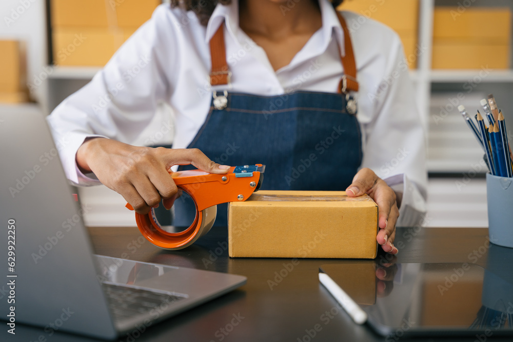 Fotka „Startup small business owner working at home, sealing cardboard ...