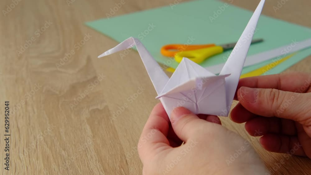 close-up of colored paper, female hands fold Japanese crane figurine in ...