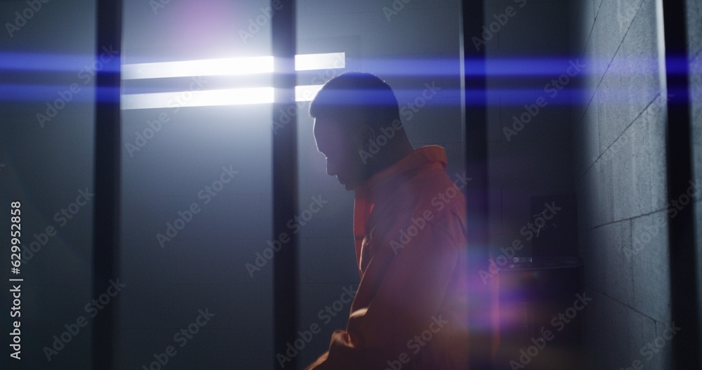 Depressed African American man in orange uniform stands from jail bed ...
