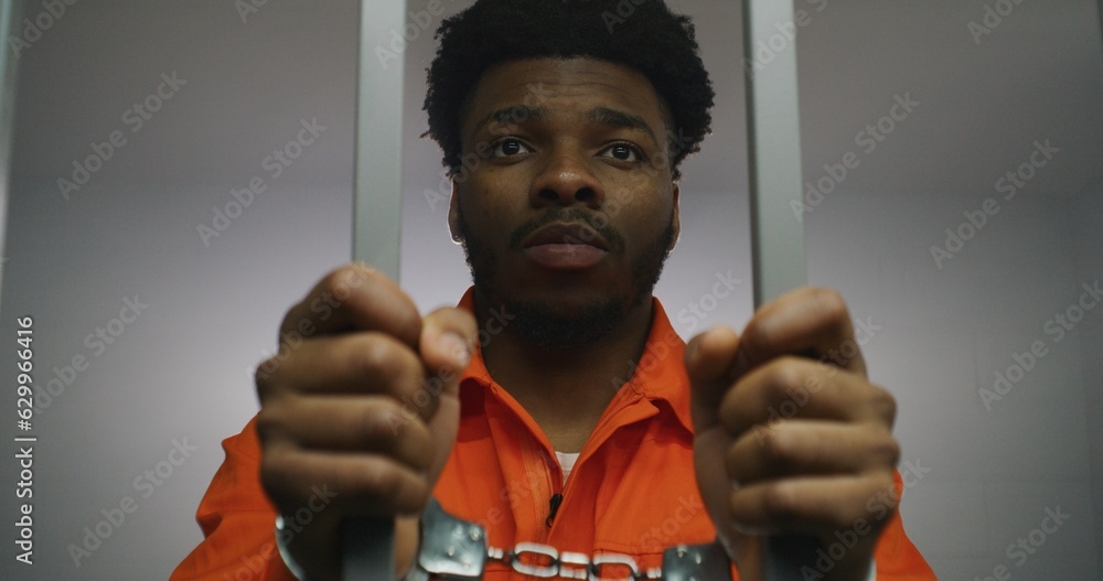 African American prisoner in orange uniform keeps hands in handcuffs on ...