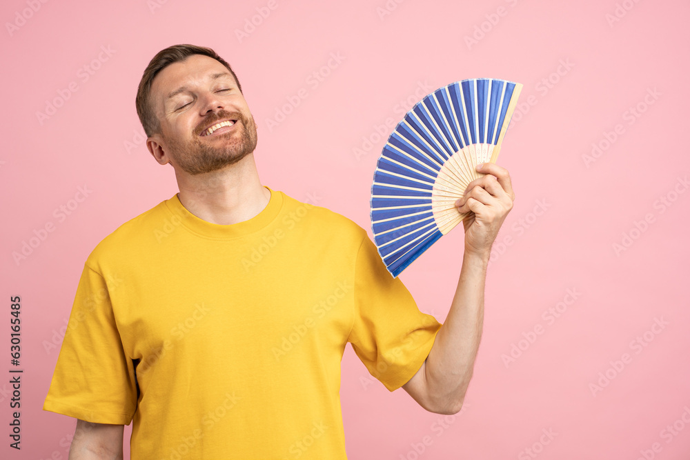 Smiling relaxed man using paper fan suffer from heat, enjoying fresh ...