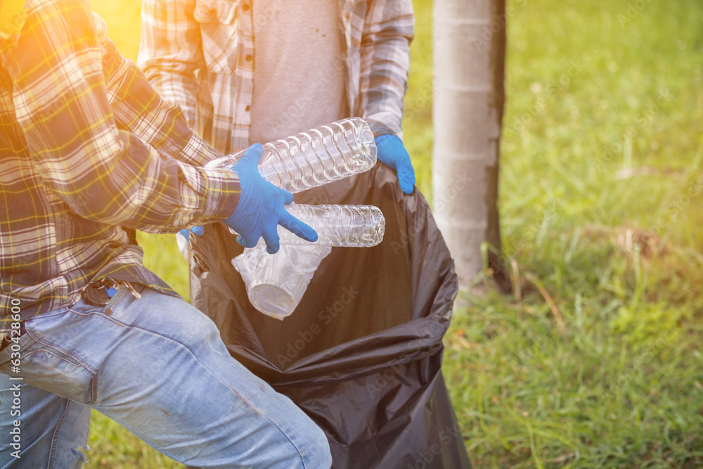 Two man employees use black garbage bags to collect plastic bottles and recyclable waste from ...