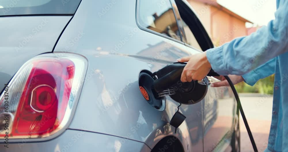 Close-up. Woman plugs in charger into socket of her modern new electric ...
