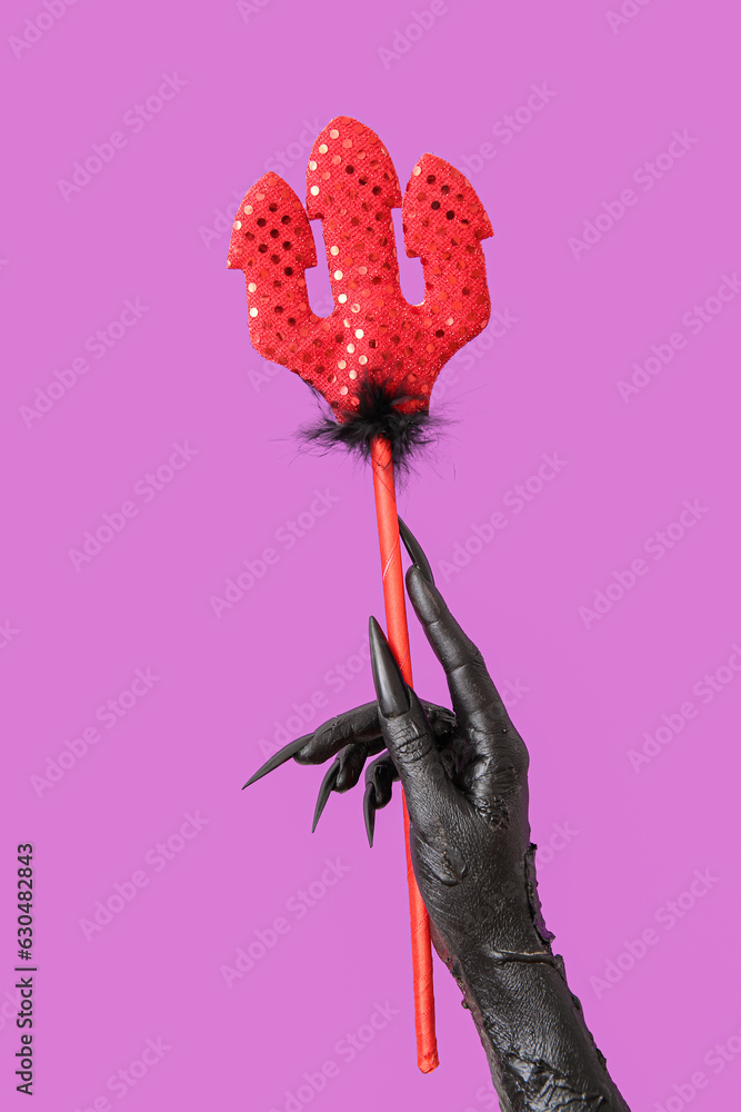 Hand of witch with red devil pitchfork on purple background. Halloween ...