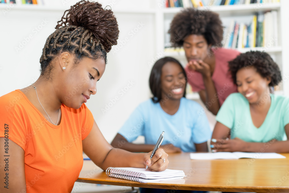 Black female student at desk writing test with group of learning ...