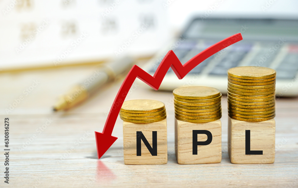 NPL on wooden cube with red arrow down icon on table with pen, calendar ...