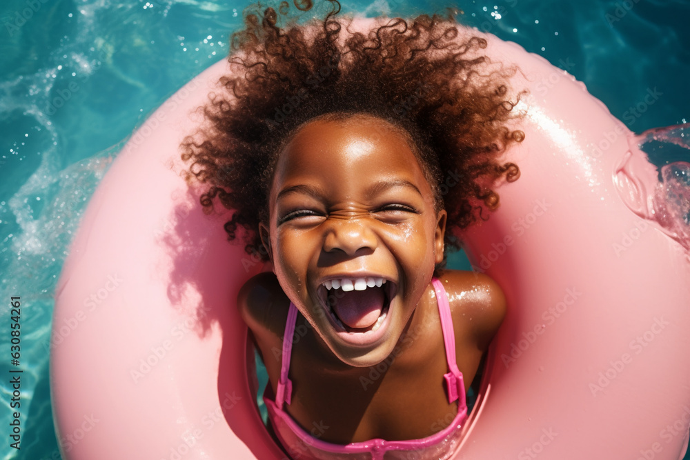 black little girl having fun and laughing floating in a pink pool float ...