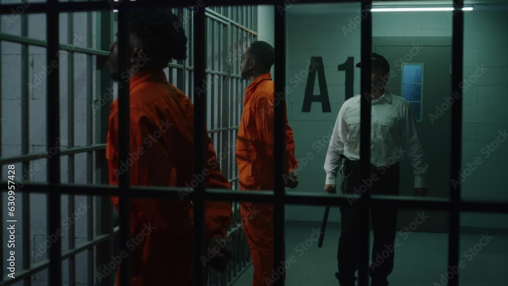 Vidéo Stock Two prisoners in orange uniforms stand facing metal bars in ...