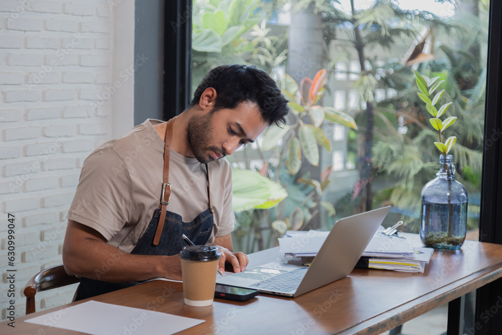 Attractive barista male or employee concentrate on stacks of tax ...