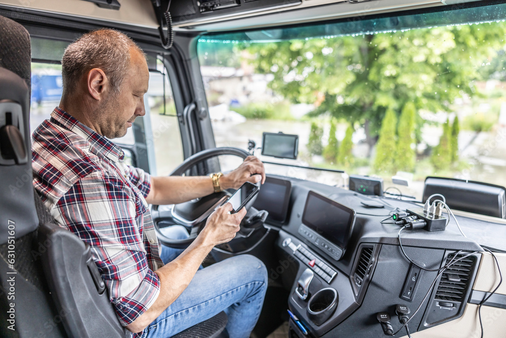 Mid-aged truck driver checks his cell phone after safely parking the ...